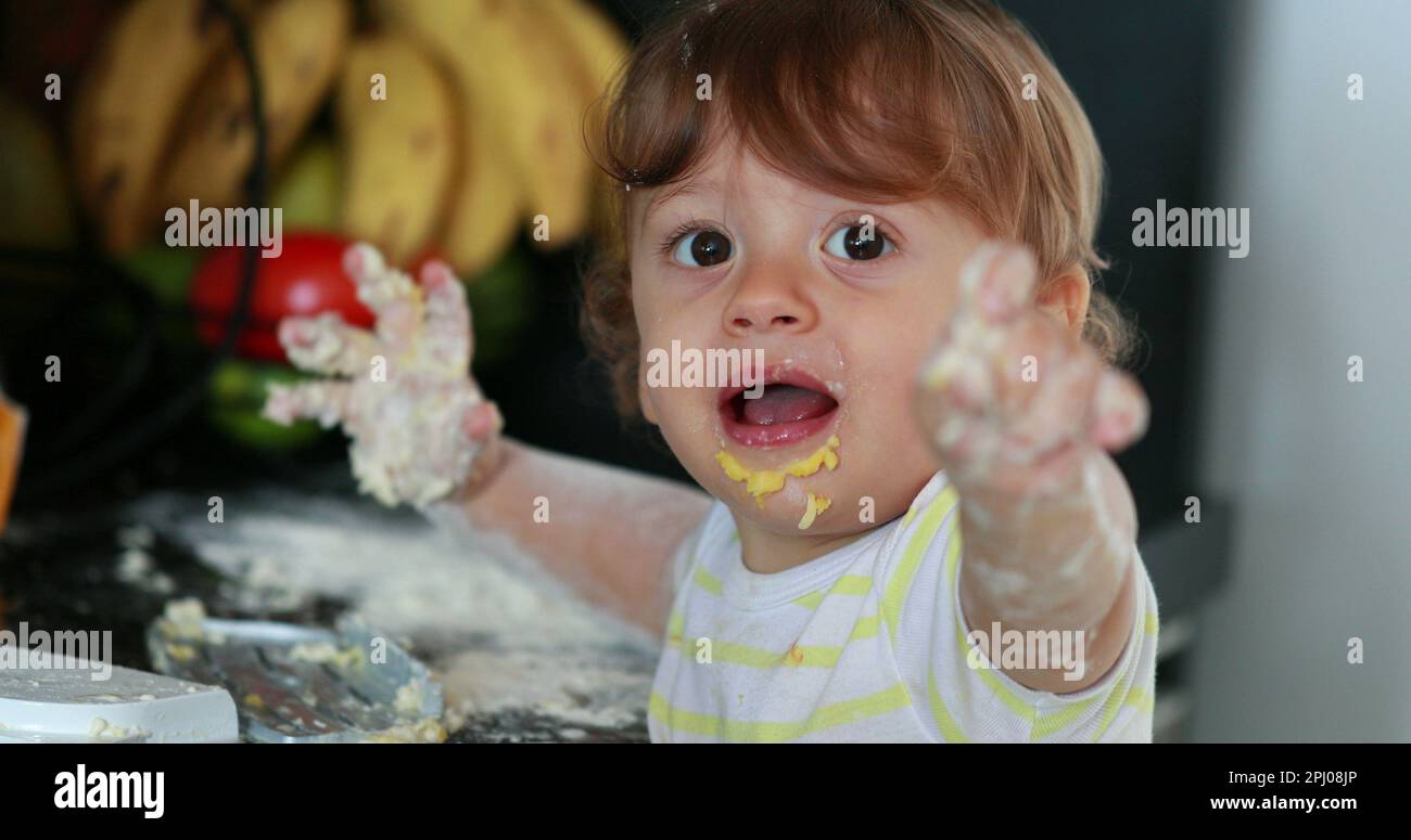 Cute messy one year old baby covered with flour at kitchen. Infant ...