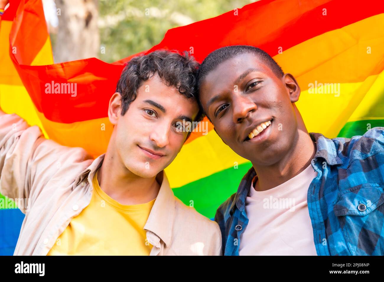 Portrait of multiethnic gay male couple holding a rainbow lgbt symbol ...