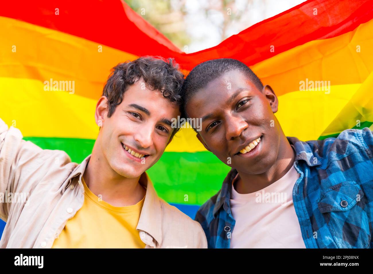 Portrait of multiethnic gay male couple holding a rainbow lgbt symbol ...
