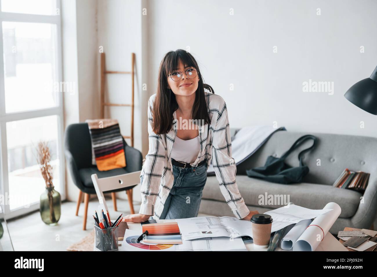 Standing near table. Young female freelance worker is indoors in home ...