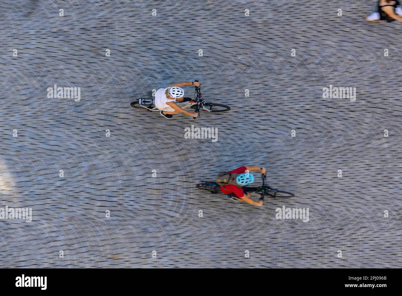 Birds eye view of people, two cyclists with helmets ride over a square ...