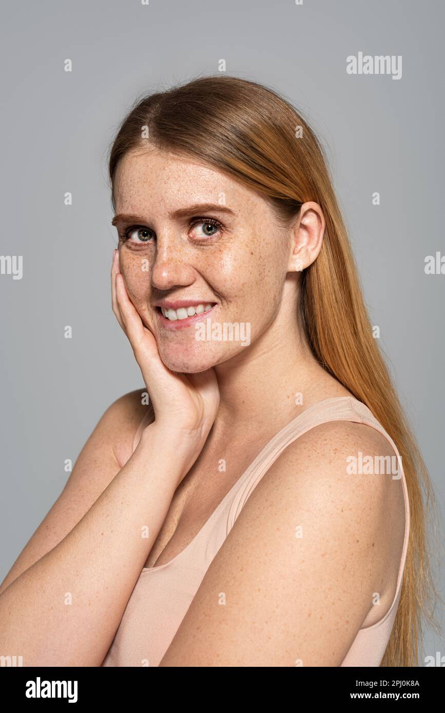 Smiling woman with freckles on face and body touching cheek isolated on ...