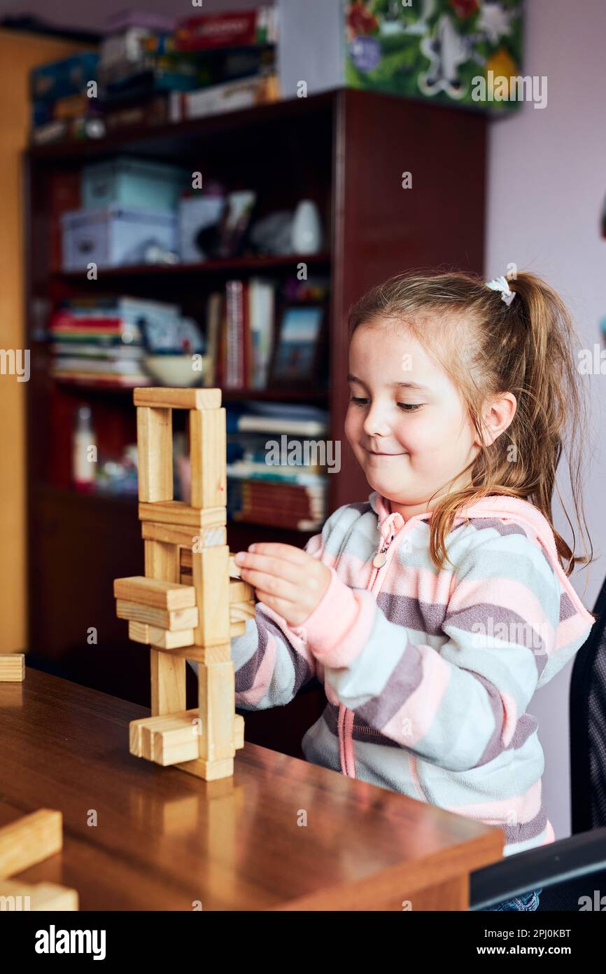 Little girl preschooler playing with wooden blocks toy building a tower ...