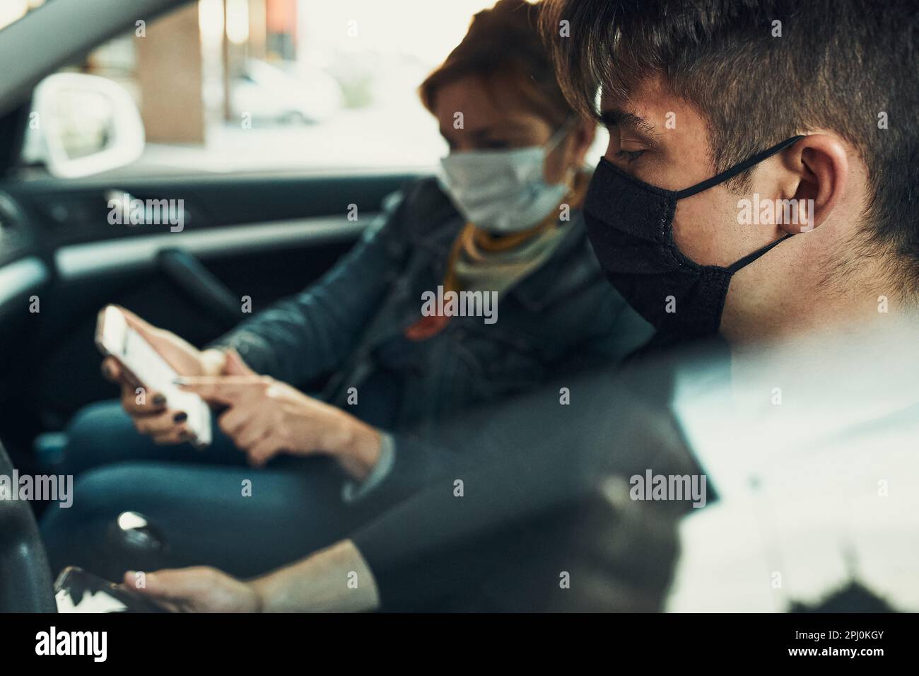 Man and woman sitting in a car using smartphones wearing the face masks ...