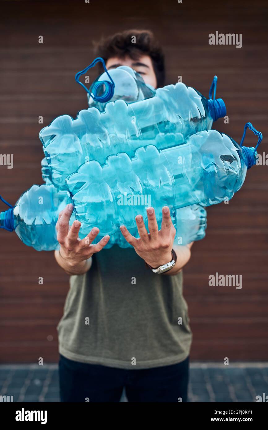 Young man throwing out empty used plastic water bottles into trash bin ...