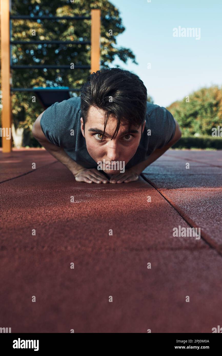 Young man doing push-ups on a red rubber ground during his workout in a ...