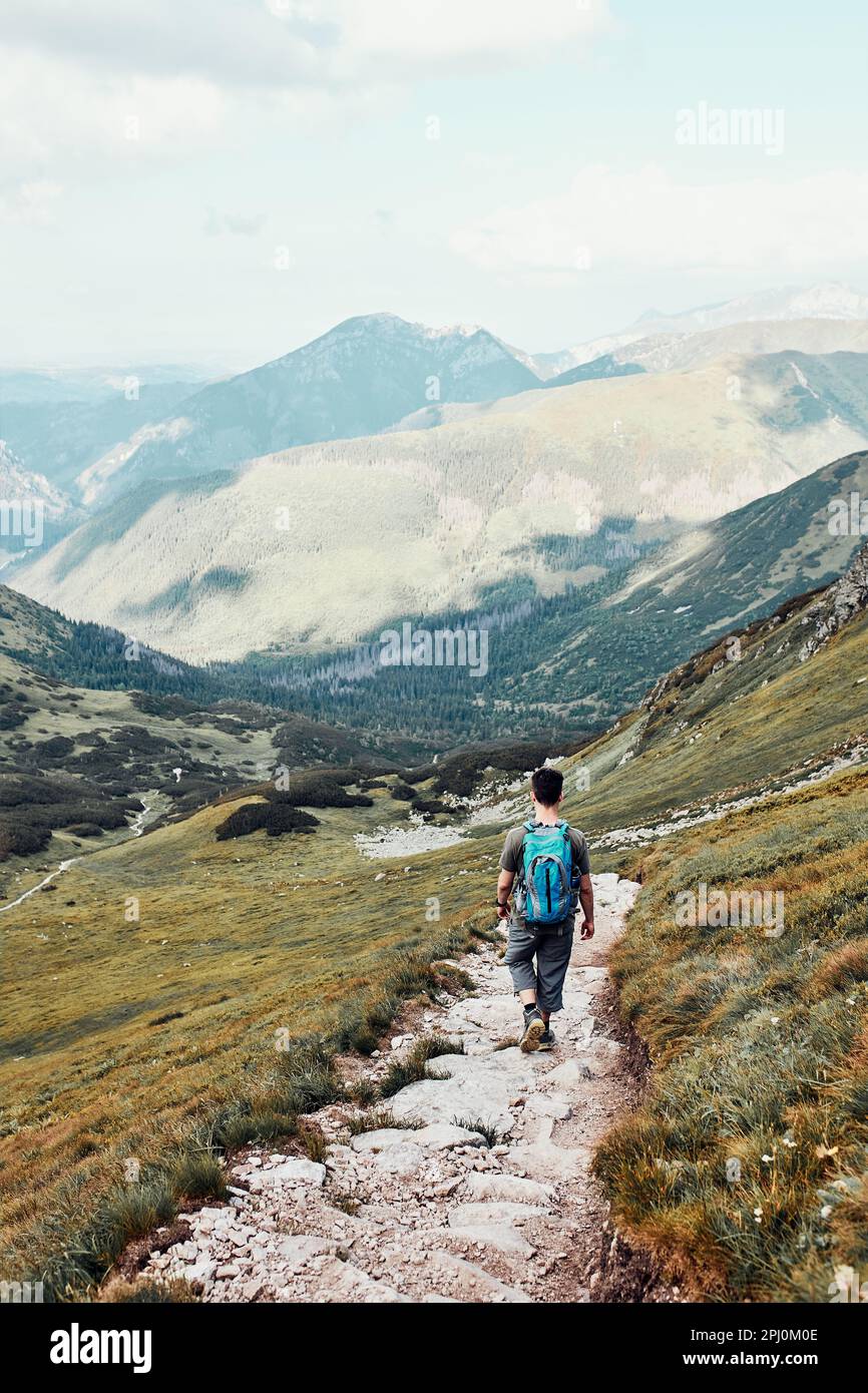 Young man with backpack hiking in a mountains, actively spending summer ...