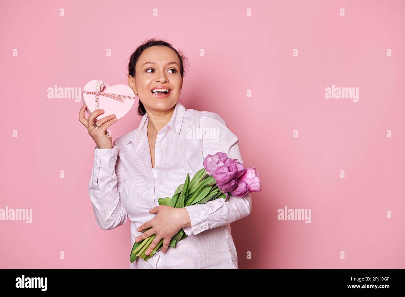 Attractive woman with bouquet of tulips, shaking a gift box, trying to ...