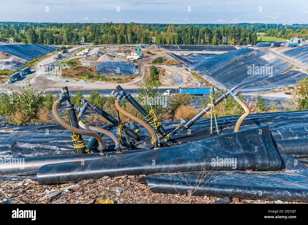 Four methane gas well heads poke out of a geomembrane overlooking hills ...
