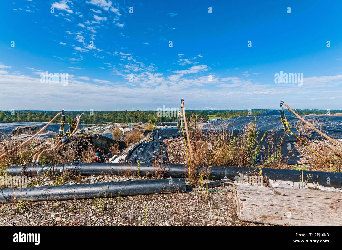Five methane gas well heads poke out of a geomembrane overlooking hills ...