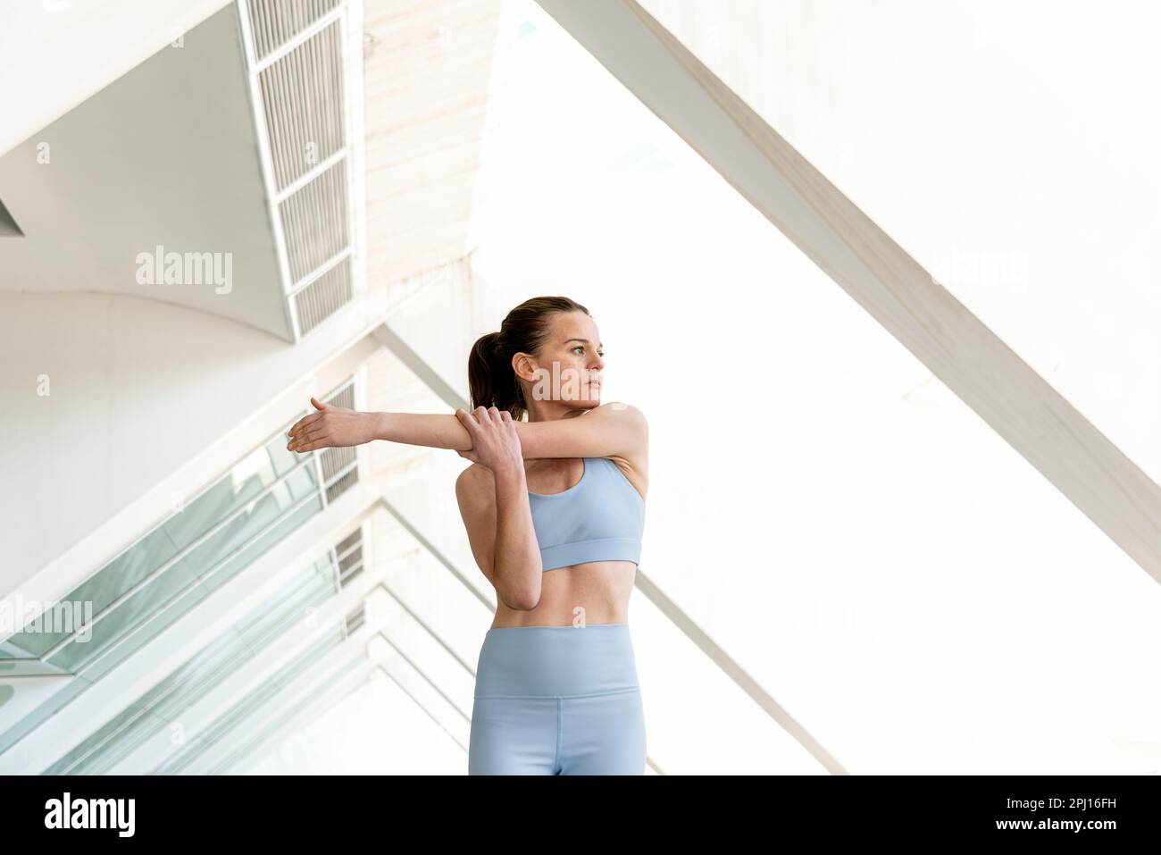 Fit, mid adult woman doing an arm stretch warm up exercise wearing blue ...