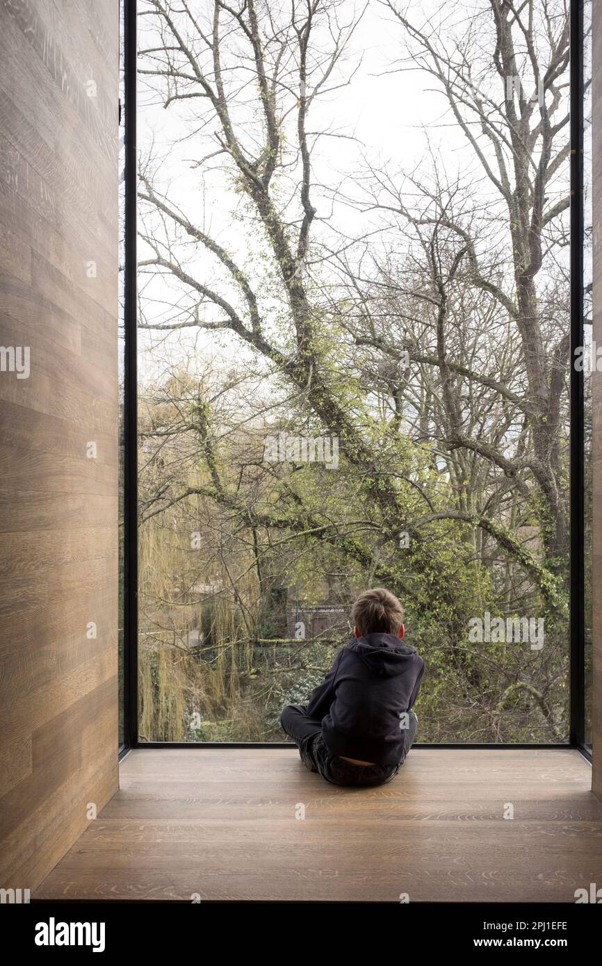 A rearview of a young boy as he sits cross legged looking out of a ...