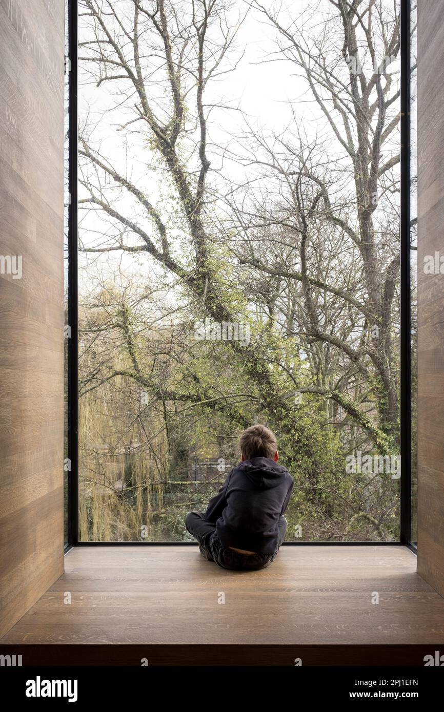 A rearview of a young boy as he sits cross legged in a wood panelled ...