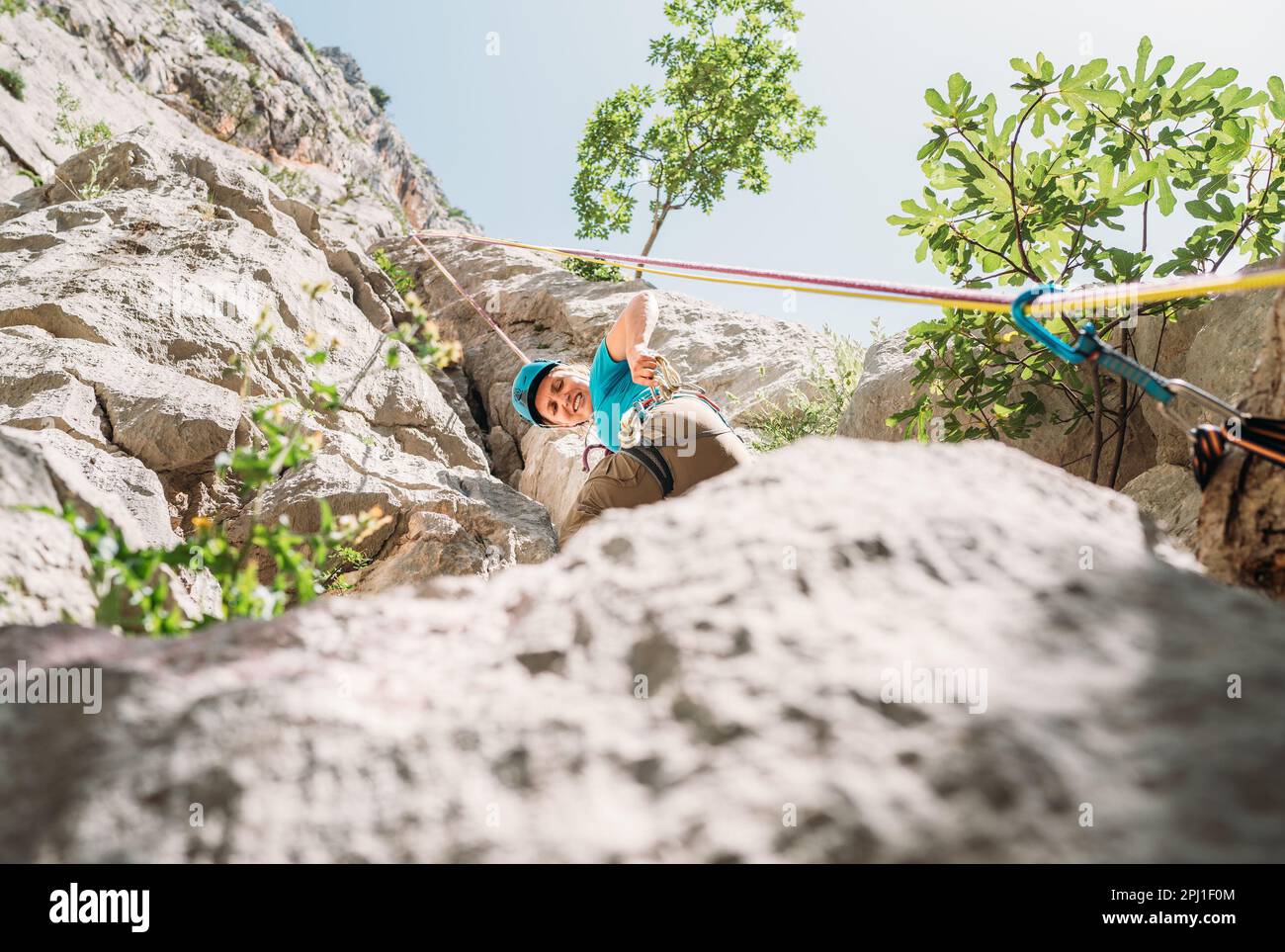 Smiling athletic woman in protective helmet climbing cliff rock wall ...