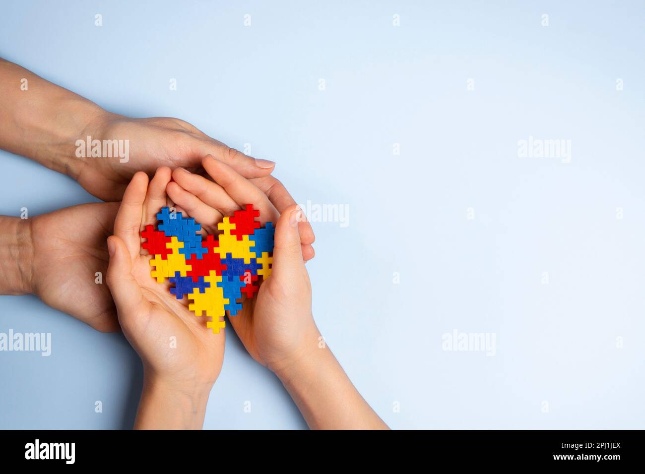 Woman and child hands holding together colorful puzzle heart on light ...