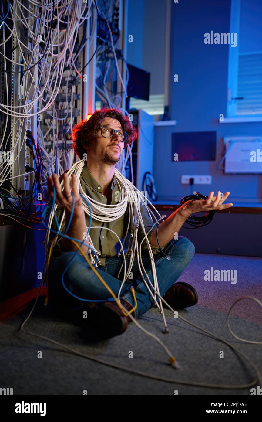 Sad, puzzled technician holding many cables in hand trying to solve ...