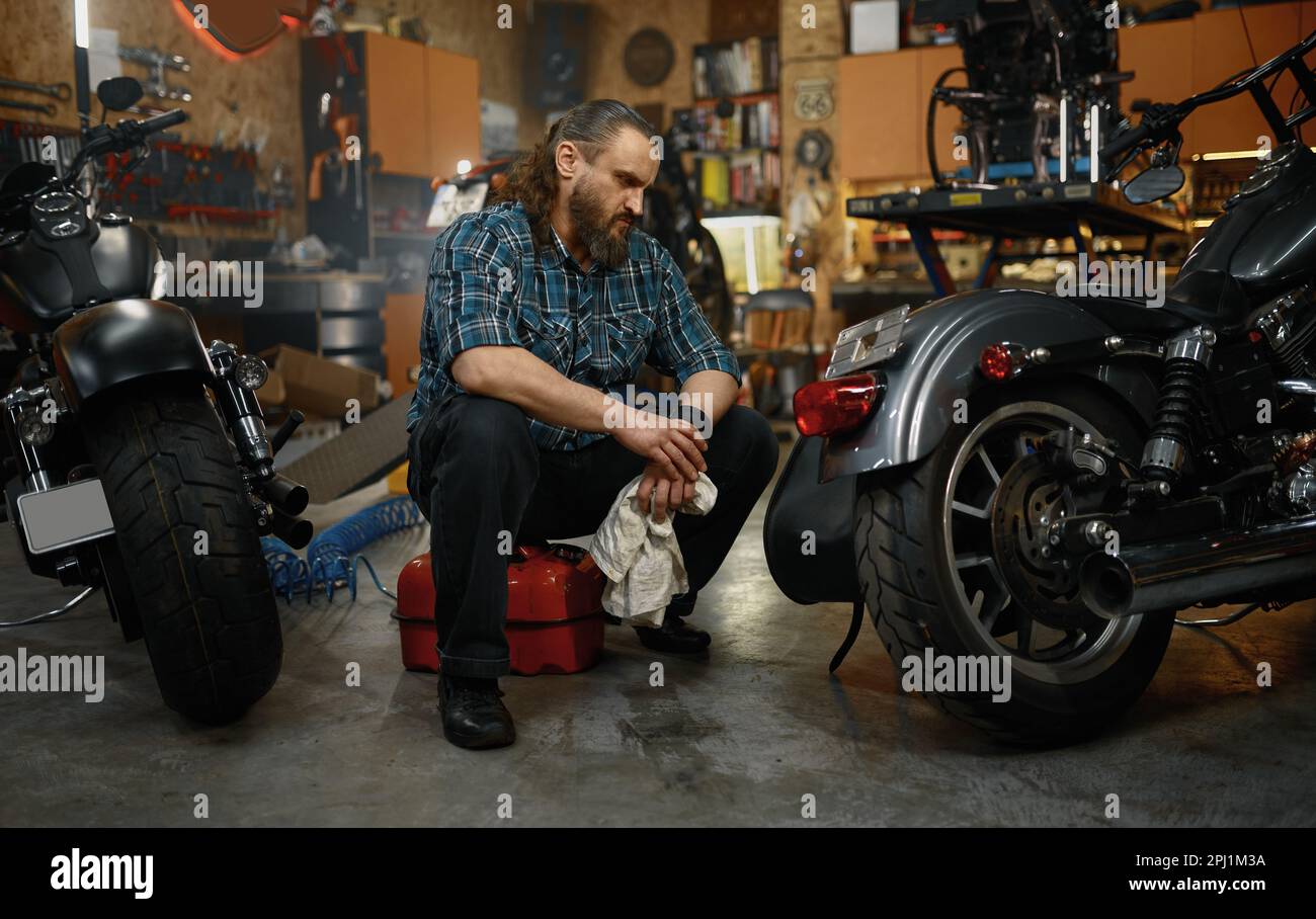 Bearded mature man biker cleaning motorcycle in garage workstation ...