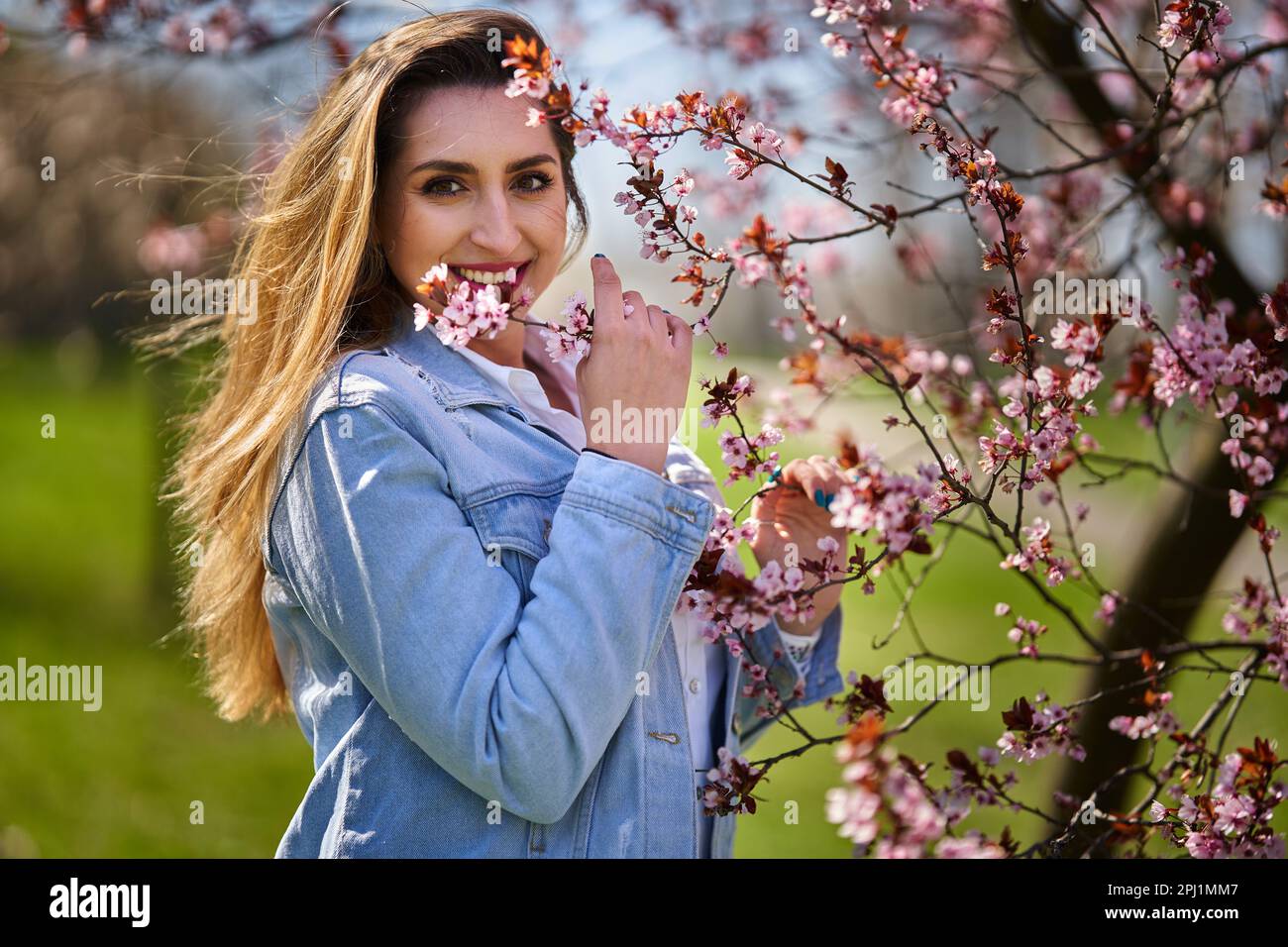 East asian young woman enjoying spring in a park with flowering trees ...