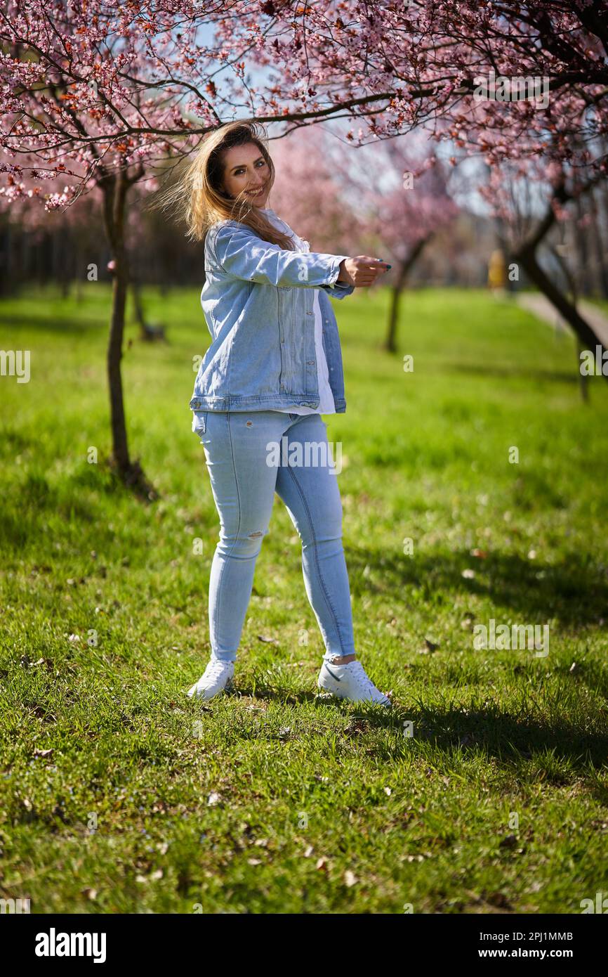 East asian young woman enjoying spring in a park with flowering trees ...