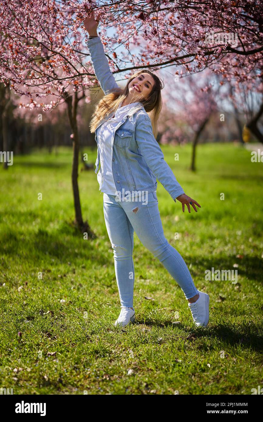 East asian young woman enjoying spring in a park with flowering trees ...