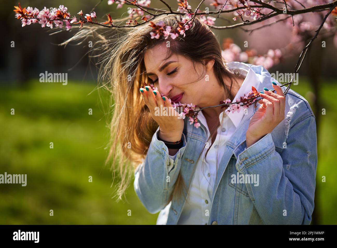 East asian young woman enjoying spring in a park with flowering trees ...