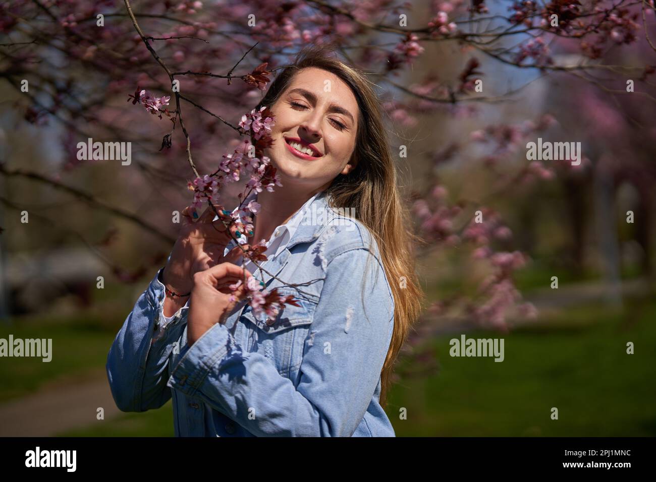 East asian young woman enjoying spring in a park with flowering trees ...