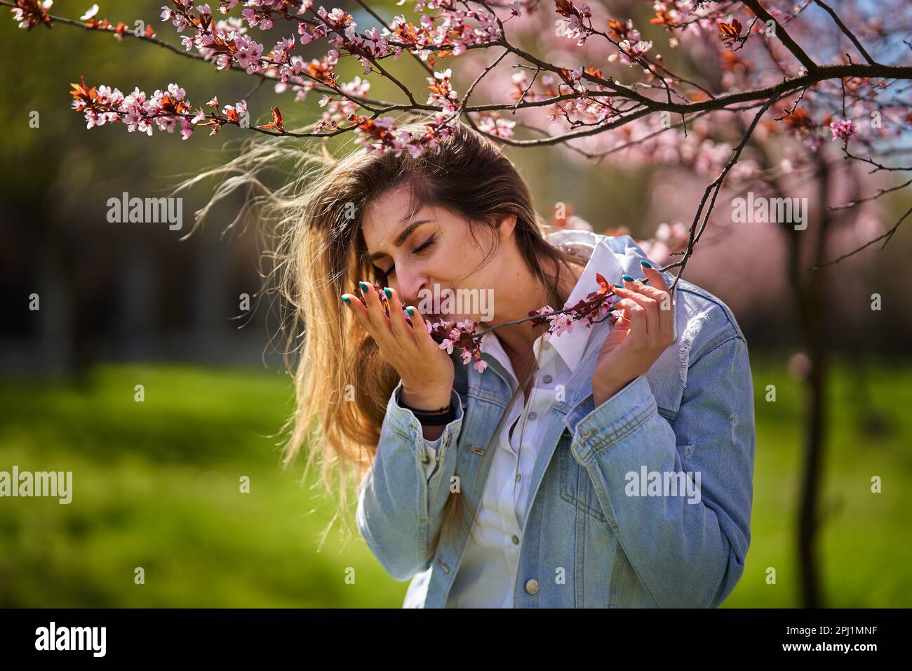 East asian young woman enjoying spring in a park with flowering trees ...