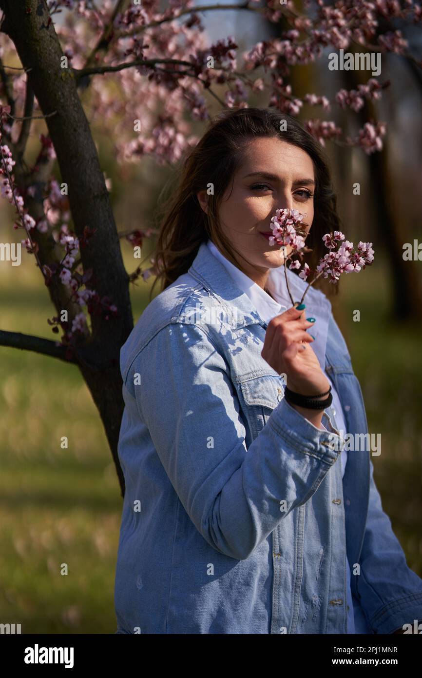 East asian young woman enjoying spring in a park with flowering trees ...
