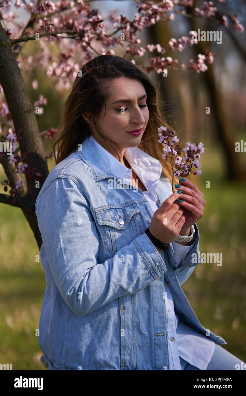 East asian young woman enjoying spring in a park with flowering trees ...