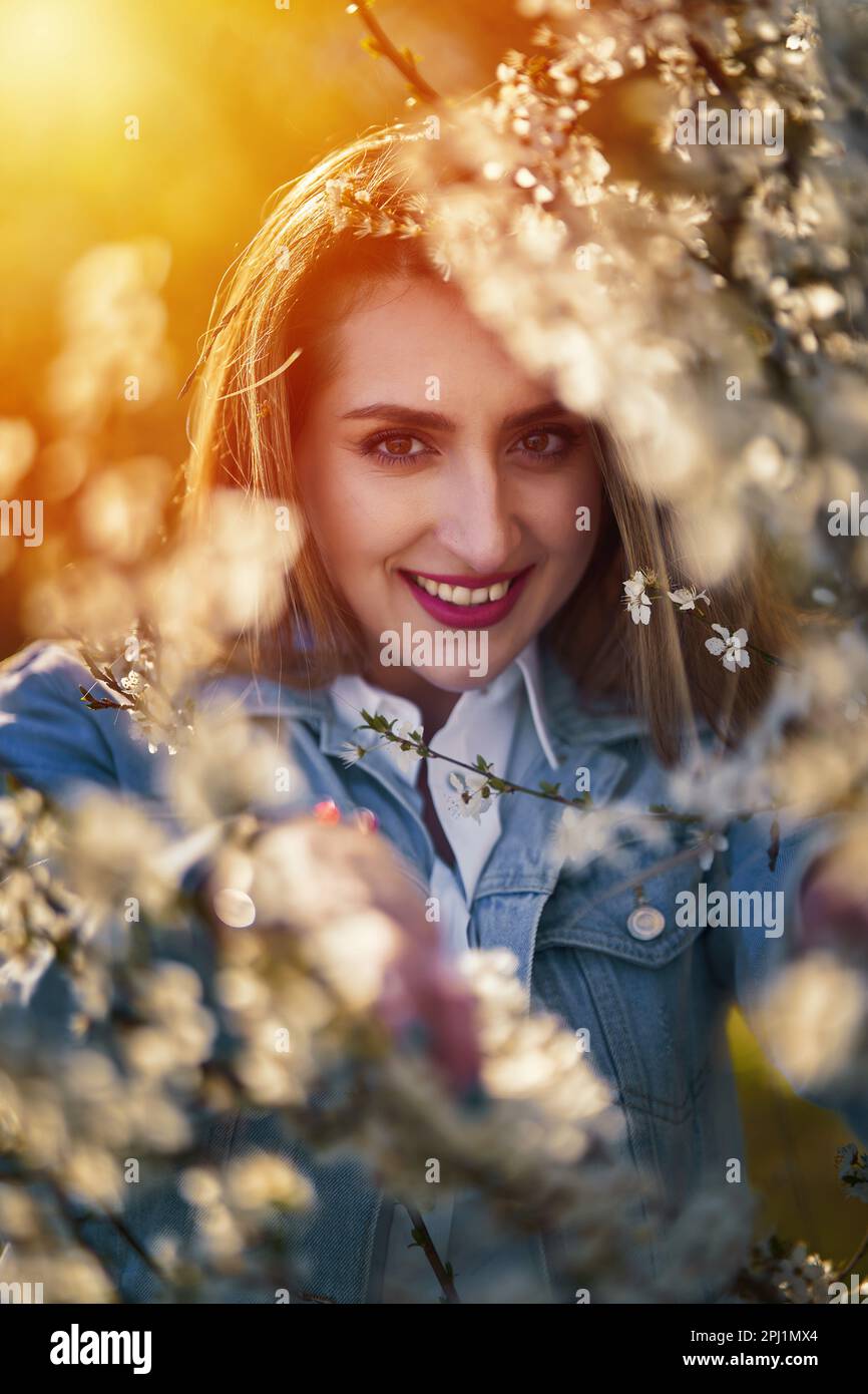 East asian young woman enjoying spring in a park with flowering trees ...