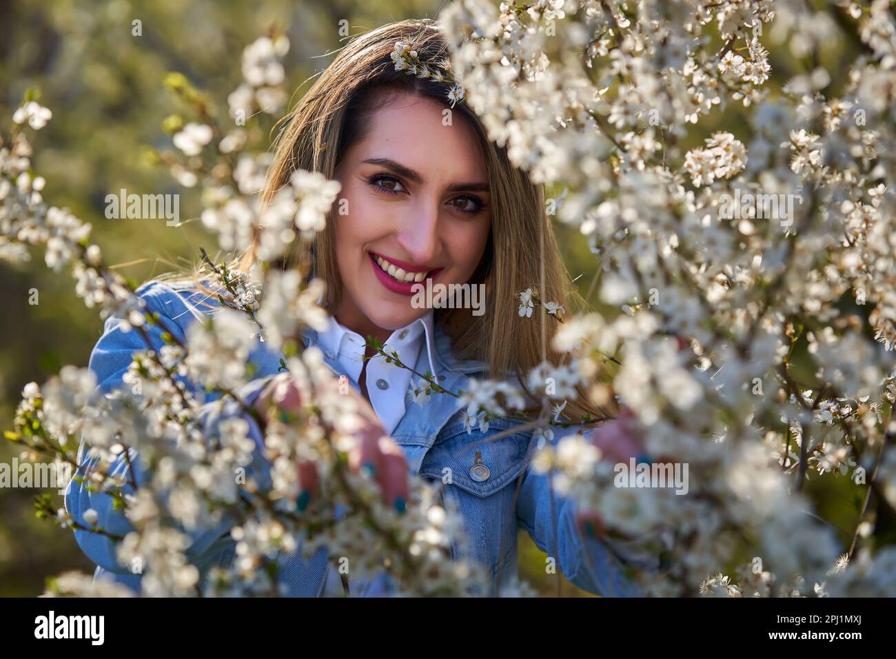 East asian young woman enjoying spring in a park with flowering trees ...