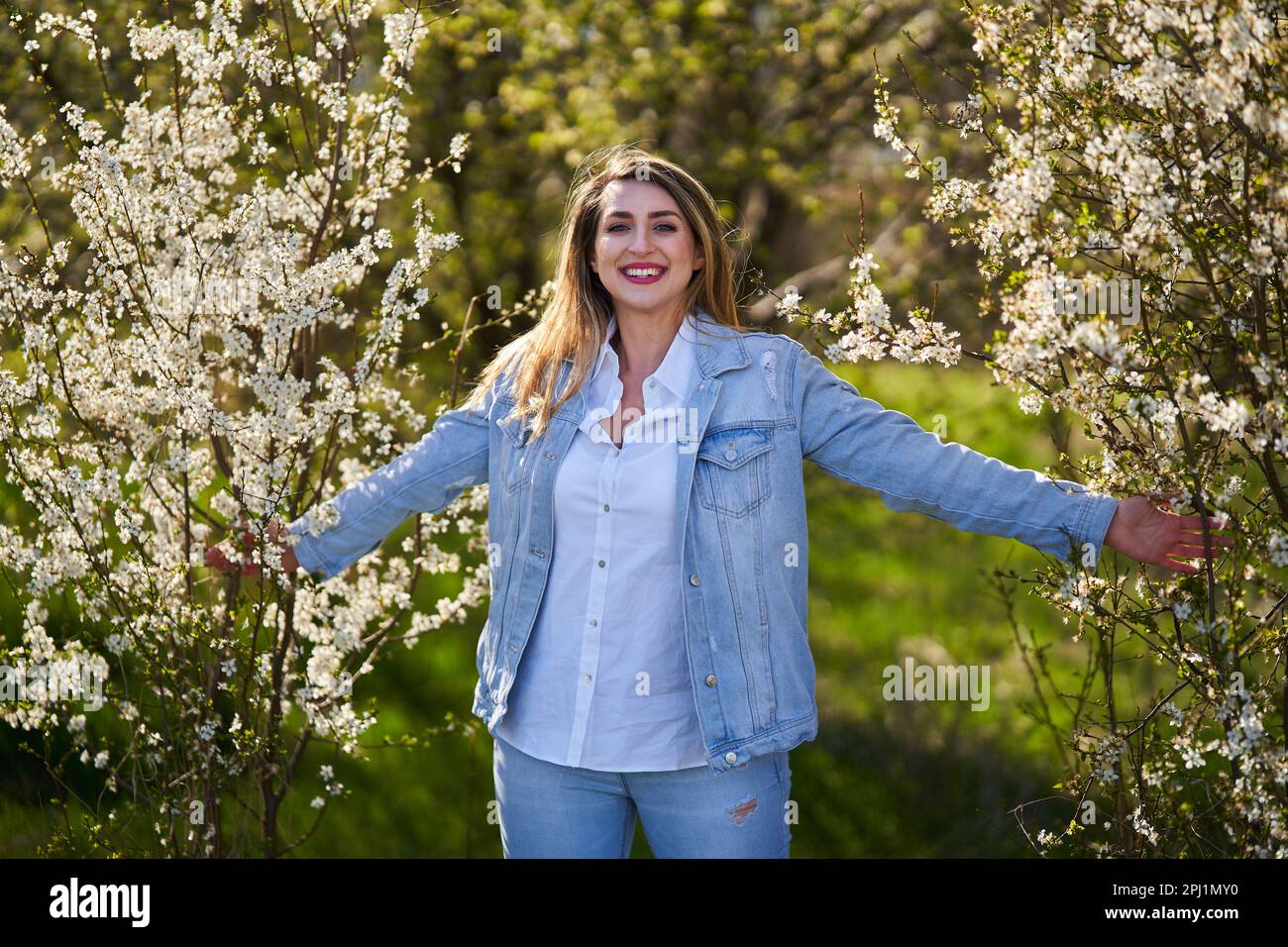 East asian young woman enjoying spring in a park with flowering trees ...