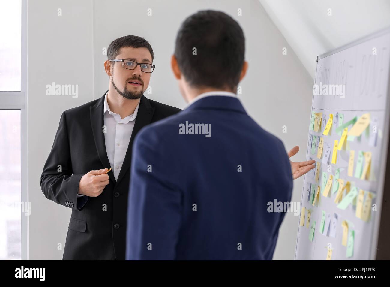 Male colleagues working on business plan near scrum task board in ...