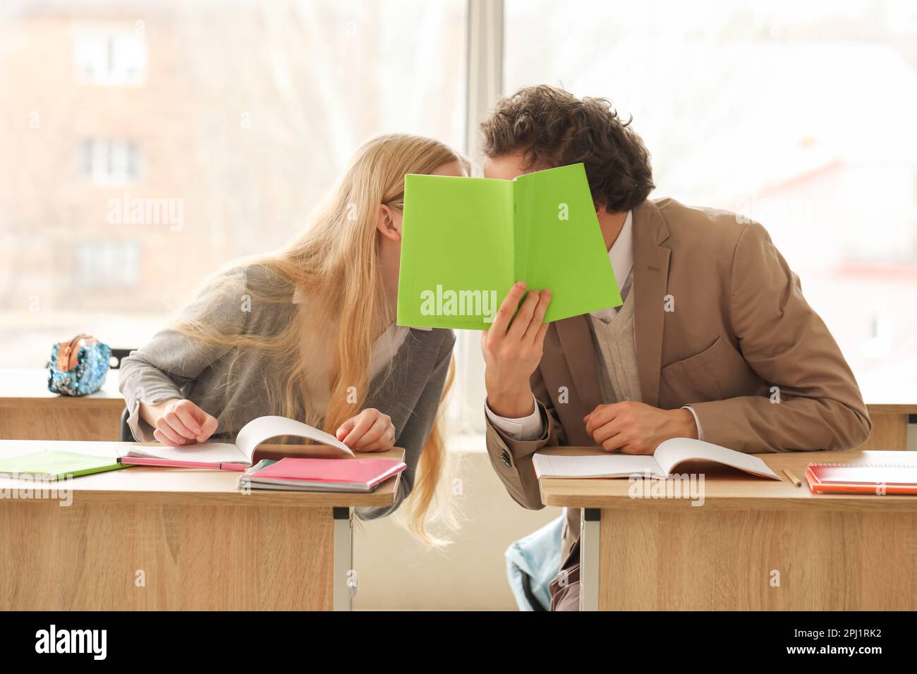 Teenage couple covering themselves with copybook in classroom Stock ...