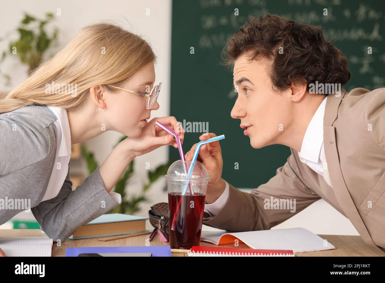 Teenage couple drinking juice with straws in classroom Stock Photo - Alamy