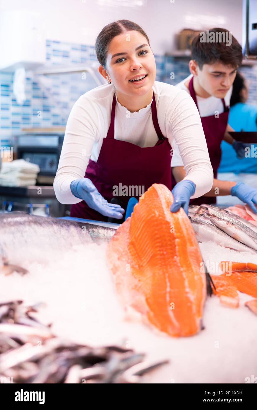 Responsive saleswoman demonstrating piece of salmon in fish store Stock ...