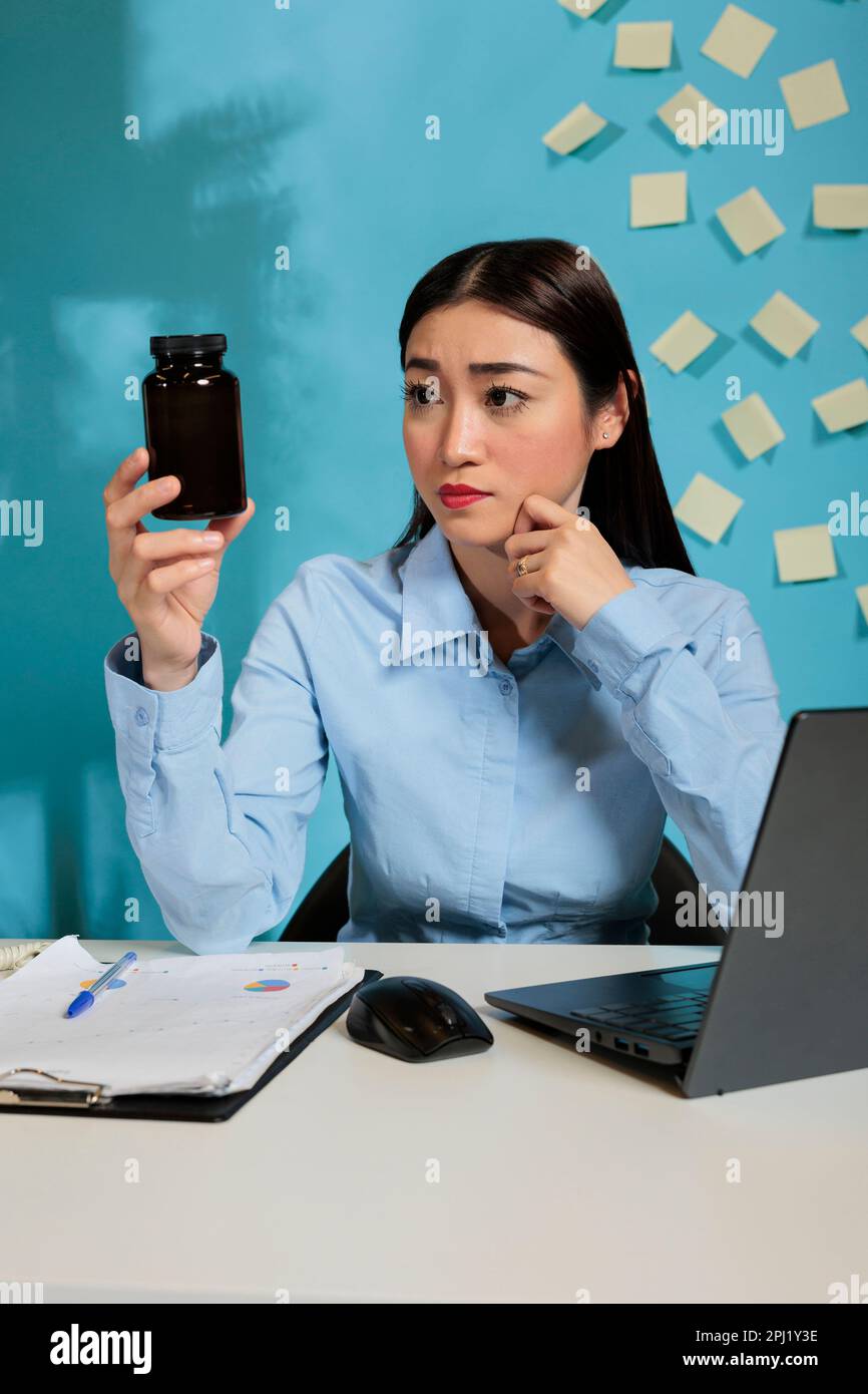 Professional asian startup employee with headache looking at bottle of ...