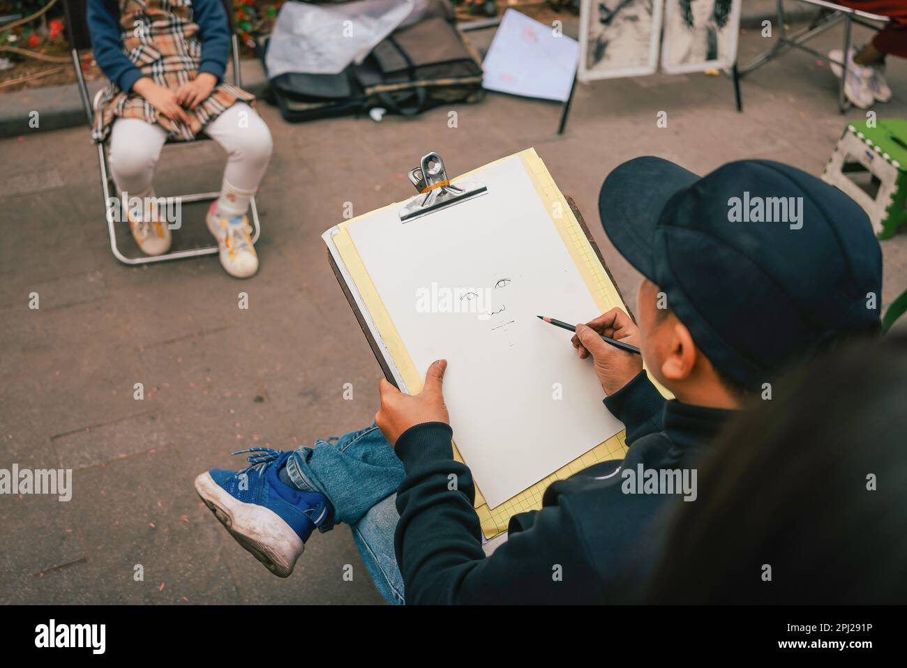 Street artist in Hanoi Vietnam from behind drawing a child. You can see ...