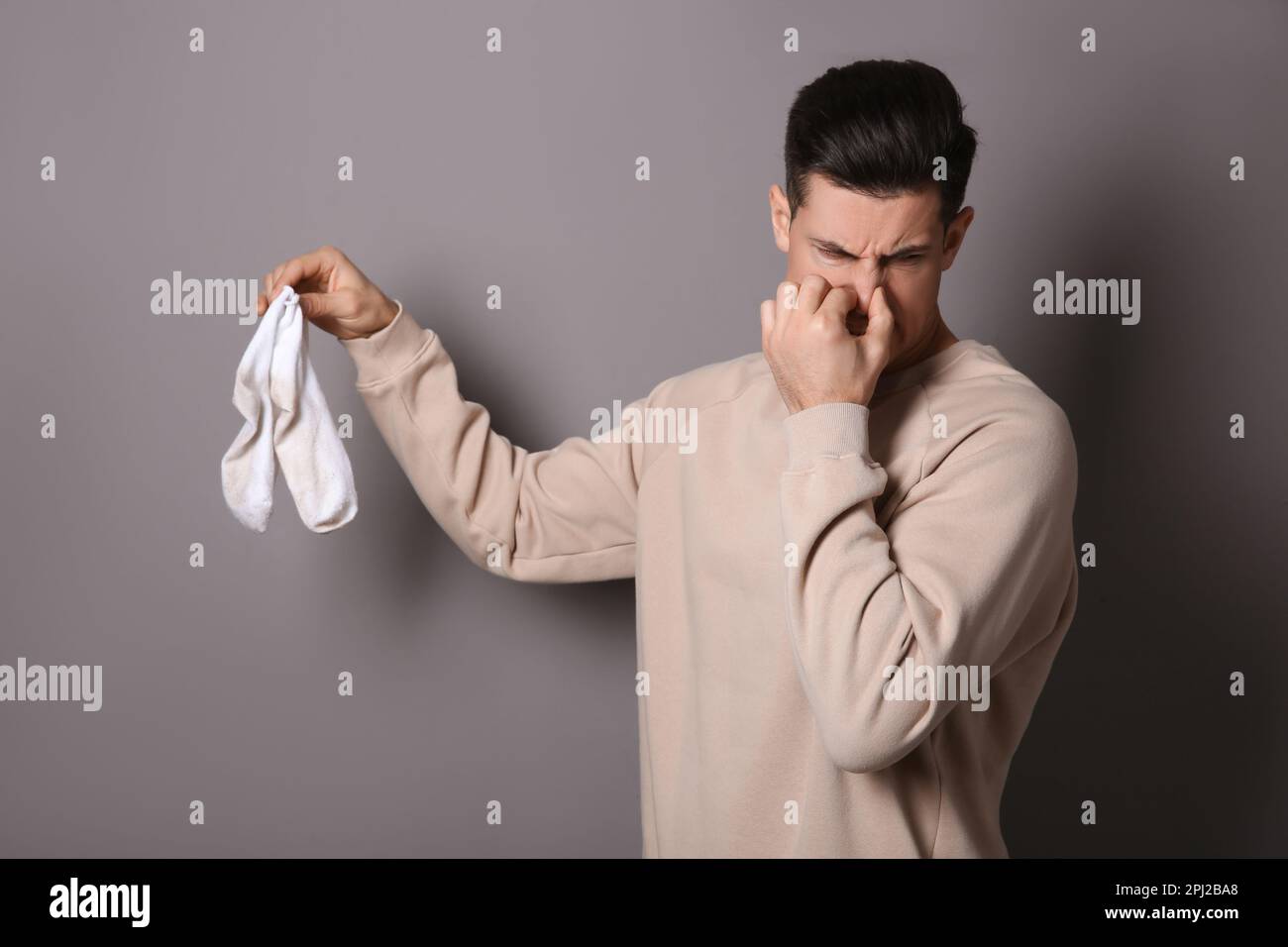 Man feeling bad smell from dirty socks on grey background Stock Photo ...