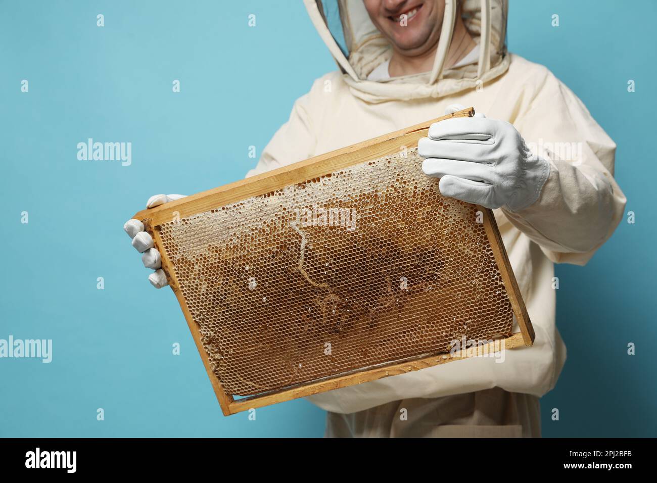 Beekeeper in uniform holding hive frame with honeycomb on light blue ...