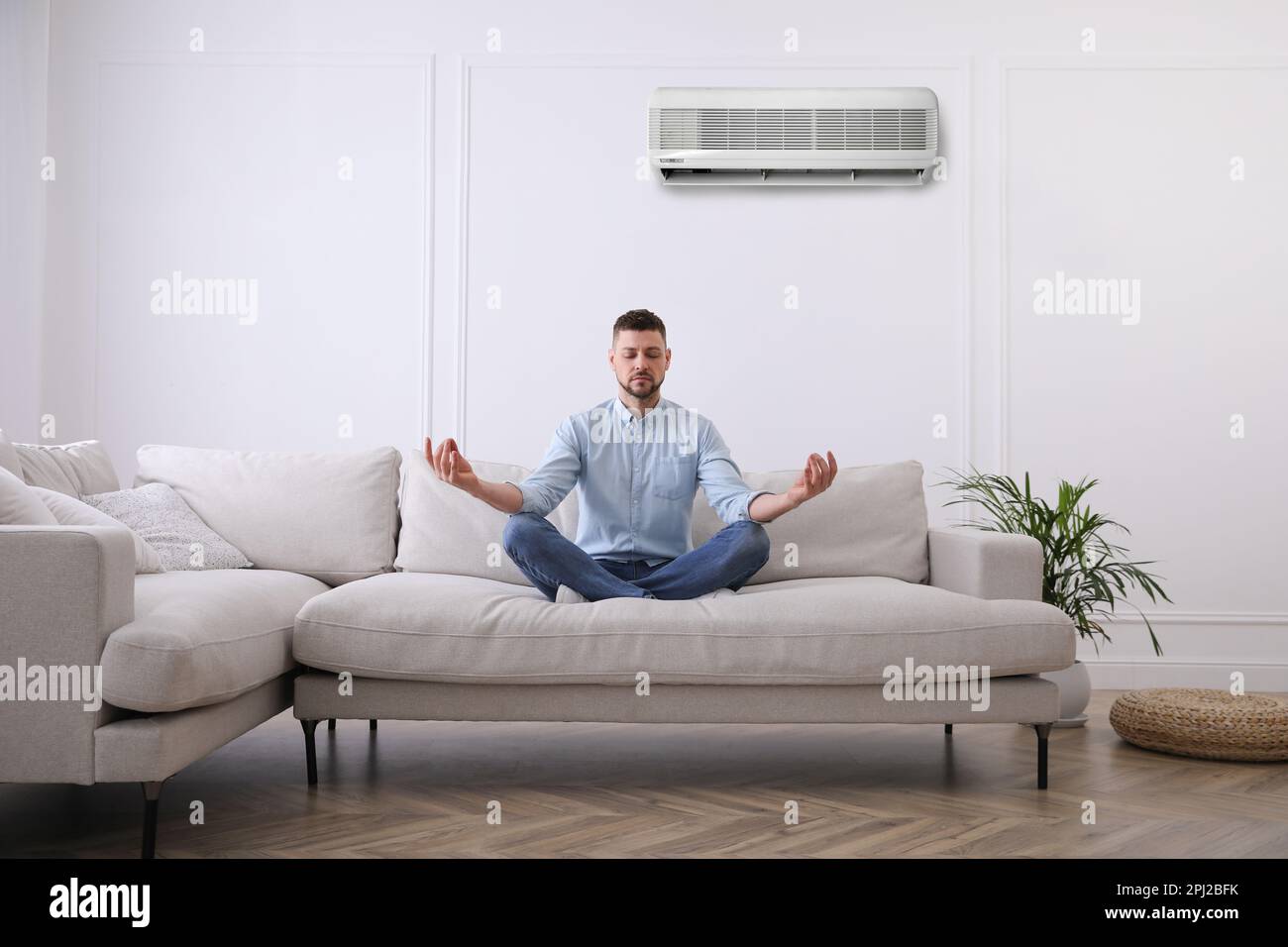 Man resting under air conditioner on white wall at home Stock Photo - Alamy