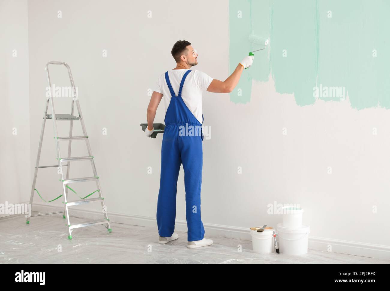Man painting wall with light blue dye indoors Stock Photo - Alamy
