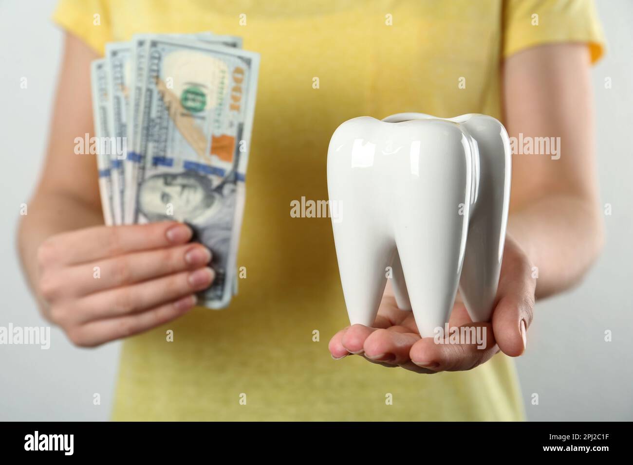 Woman holding ceramic model of tooth and dollar banknotes on light ...