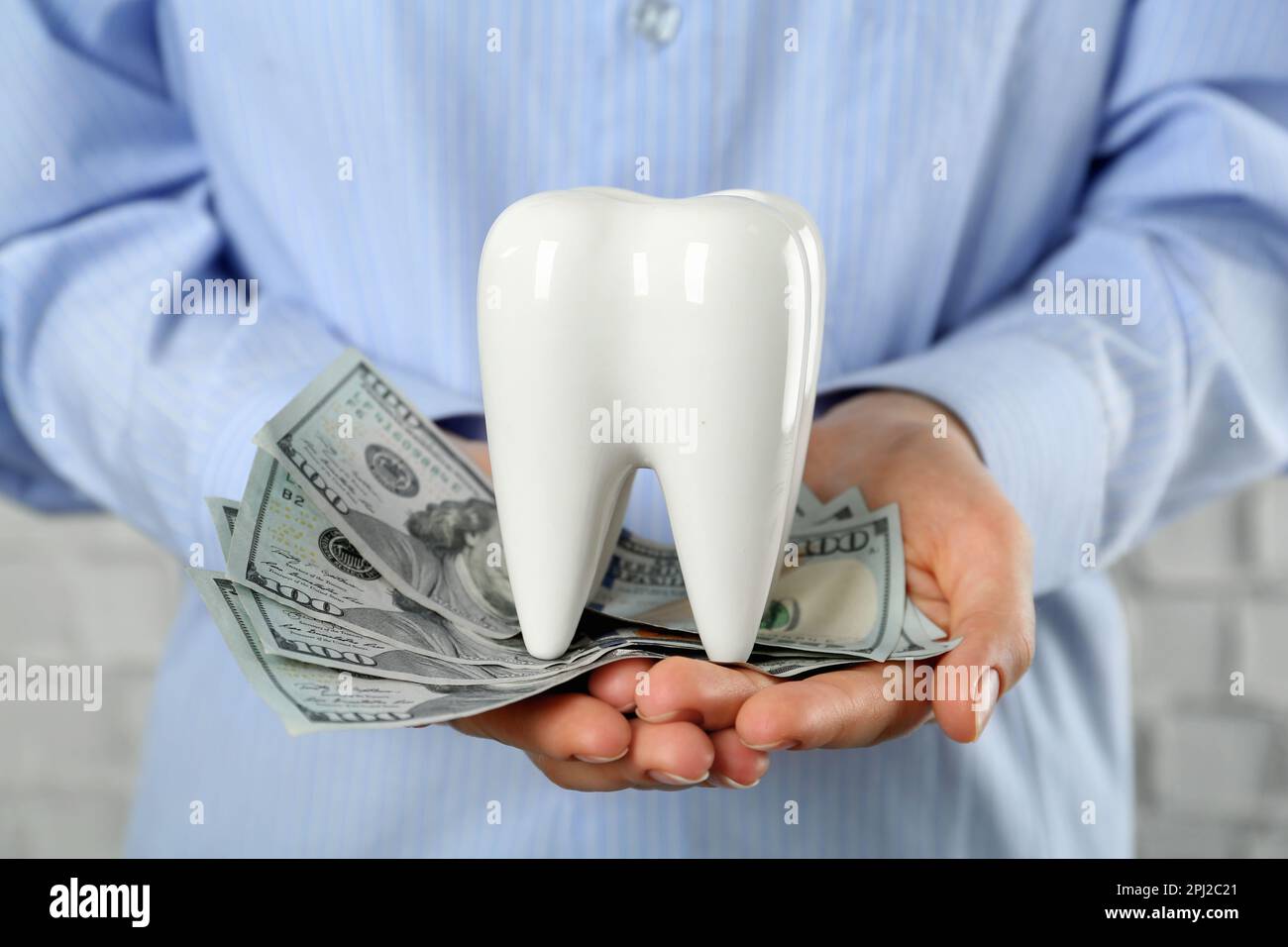 Woman holding ceramic model of tooth and dollar banknotes on light ...