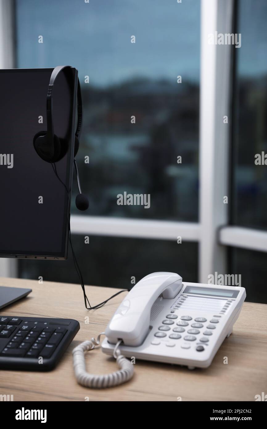 Stationary phone near modern computer with headset on wooden desk ...
