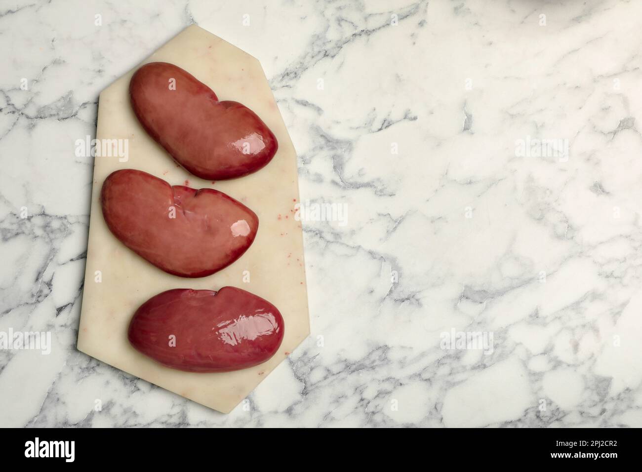 Fresh raw pork kidneys on white marble table, top view. Space for text ...