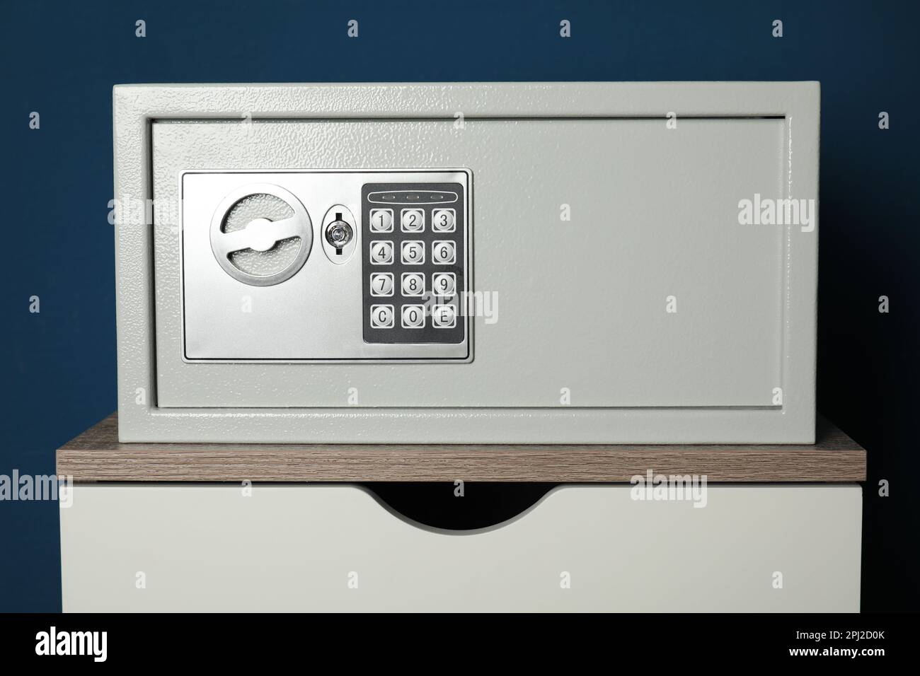 Steel safe with electronic lock on wooden table against blue background ...