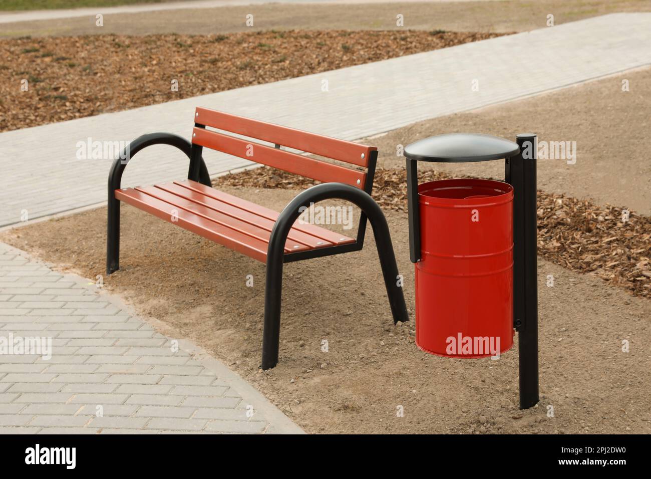 Red metal trash bin near wooden bench in city park Stock Photo - Alamy