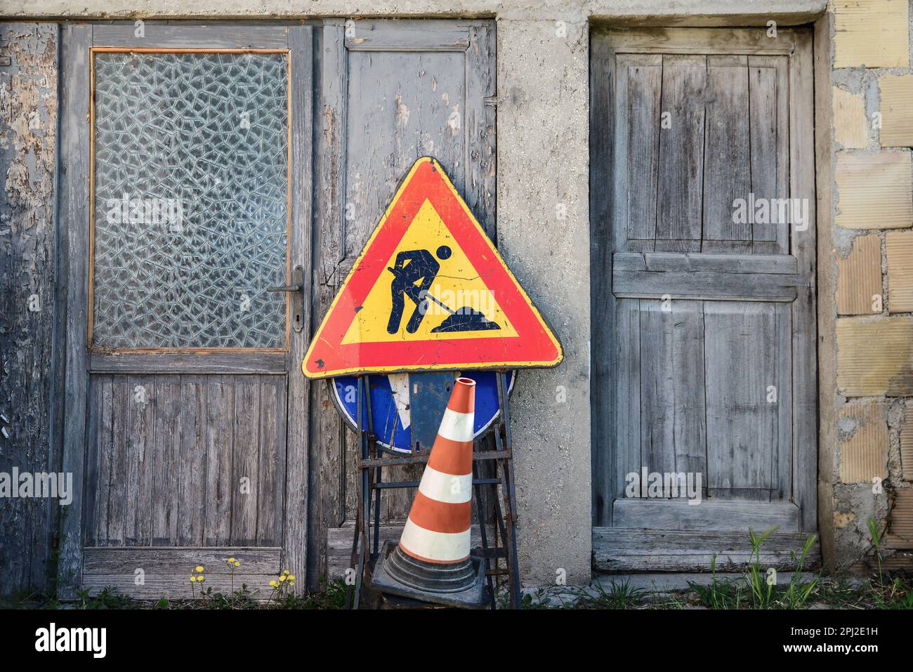 Different traffic signs and road safety cone near wooden door of old ...