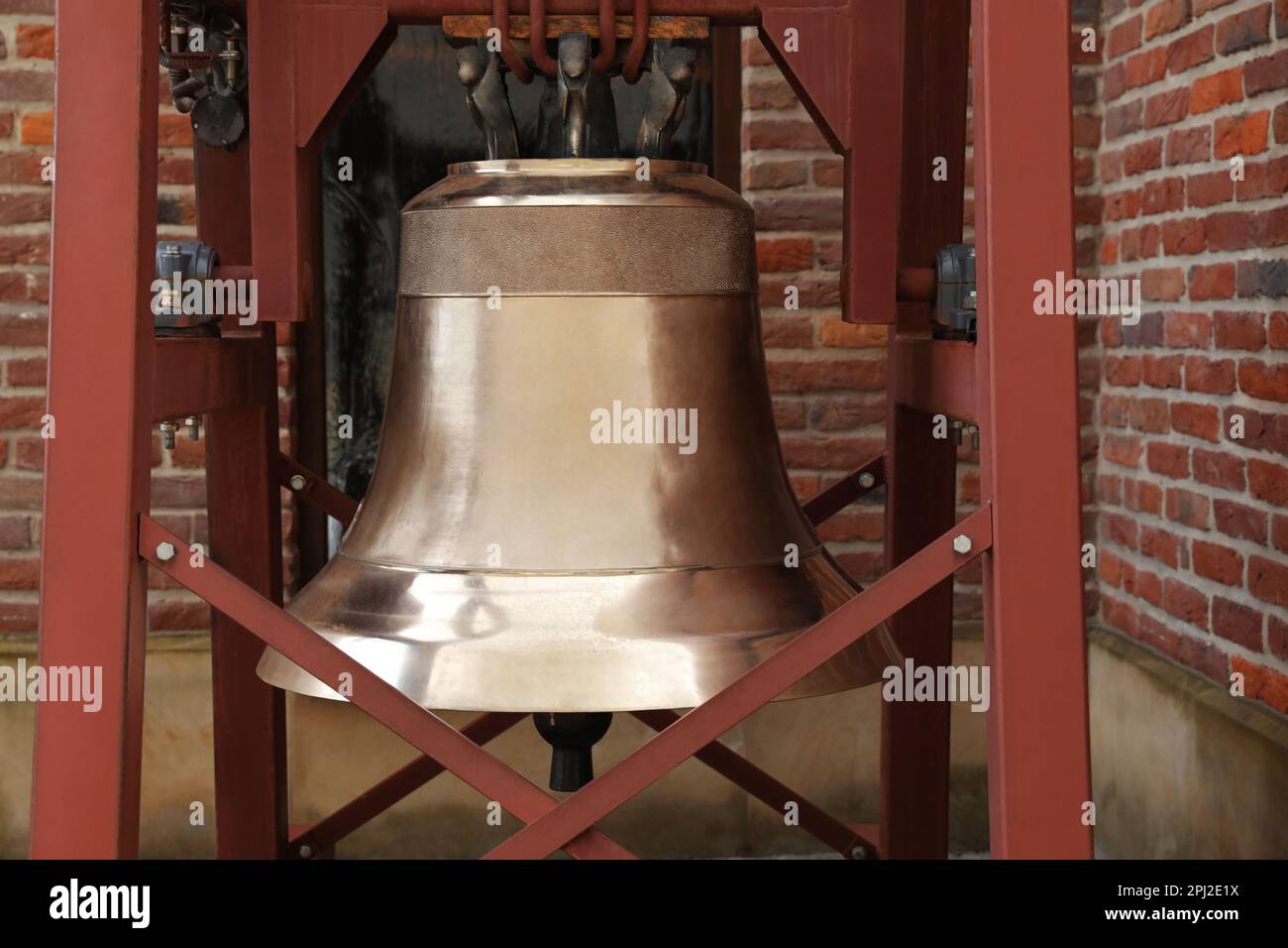 Wooden construction with large old bronze bell near brick wall outdoors ...